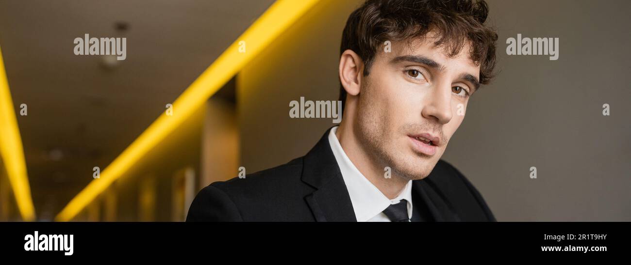 portrait of good looking and young groom in black formal wear with ...