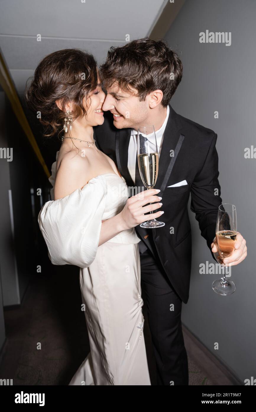 cheerful groom hugging and kissing young and brunette bride in white ...