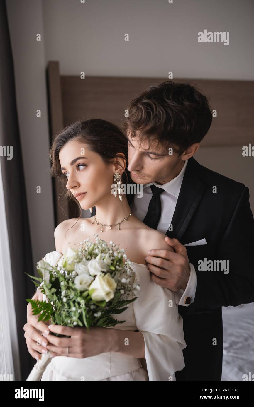 tender groom in classic formal wear touching shoulder of elegant young ...