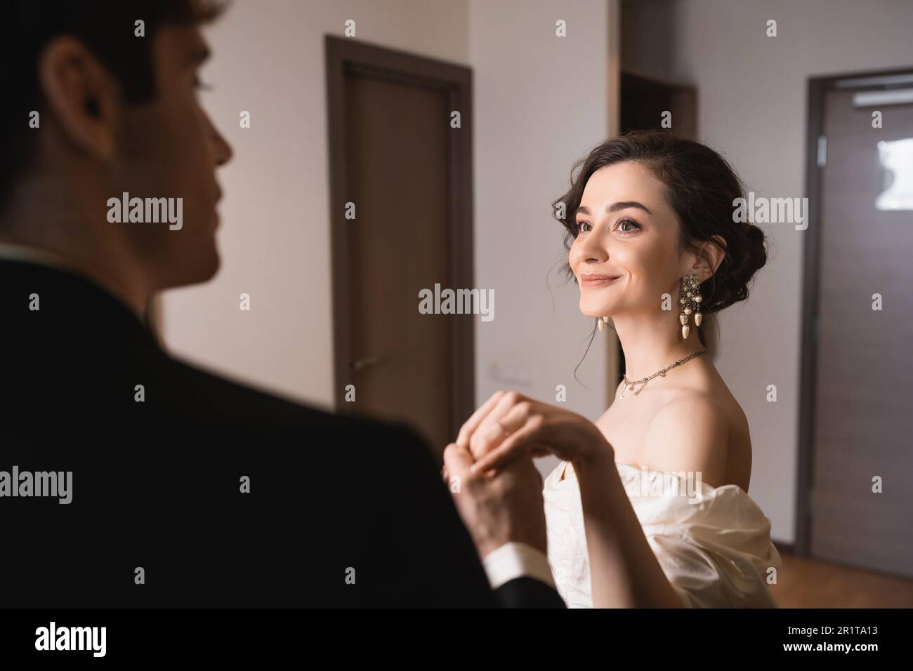 pretty young bride in elegant jewelry and white dress holding hands ...