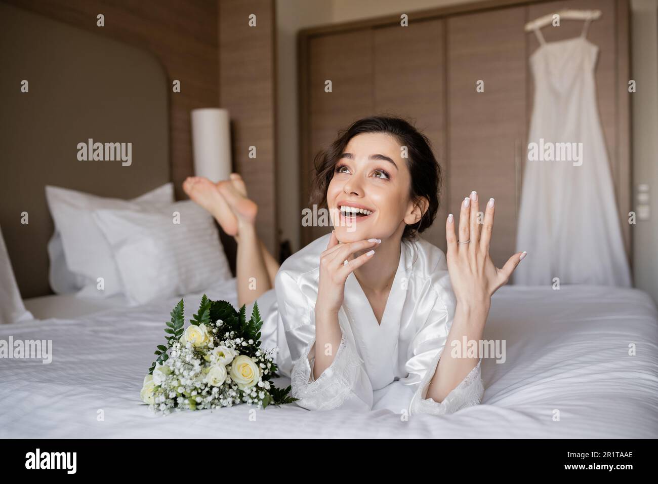 happy woman with brunette hair lying white silk robe and showing ...