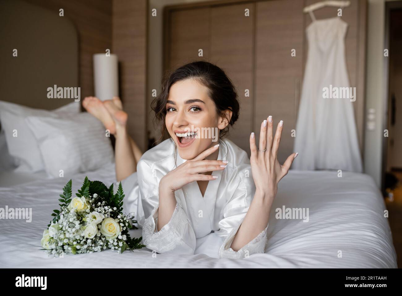 amazed woman with brunette hair lying white silk robe and showing ...