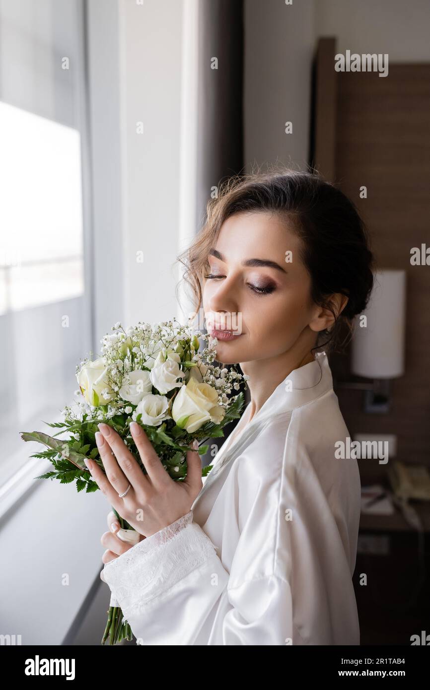 young woman with engagement ring on finger standing in white silk robe ...