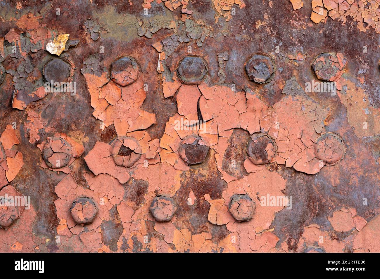 Old red paint, discoloured and flaked, on a heavily corroded rusty ...