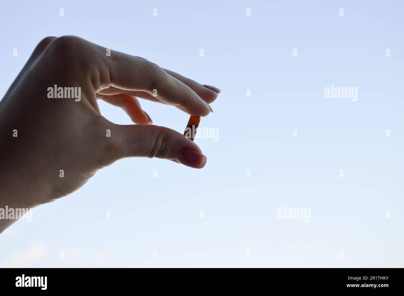 darkened hand with a brown oval tablet against the sky. medicines for ...