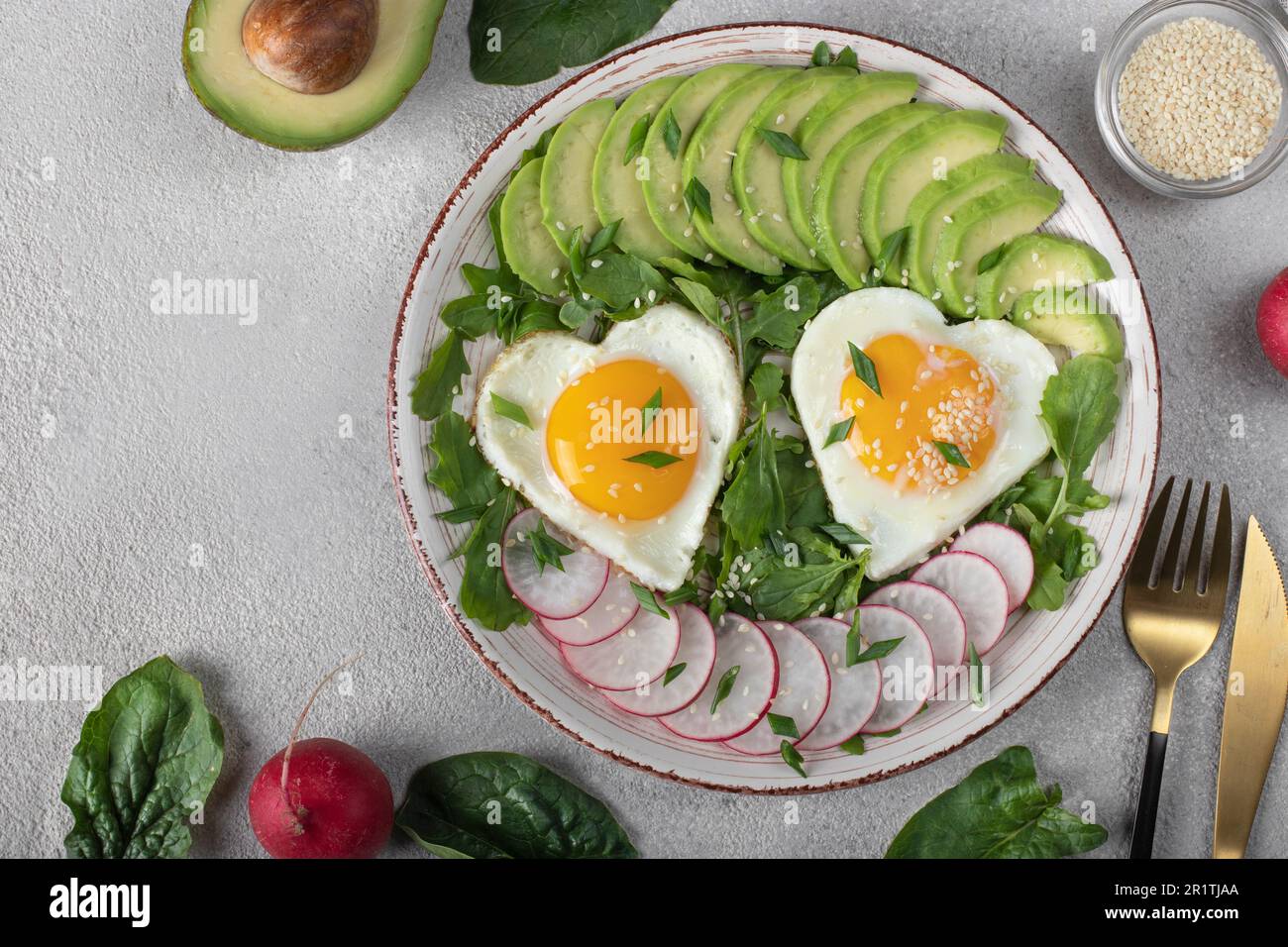 Healthy romantic breakfast - heart-shaped fried eggs served with avocado and radish, Top view ...