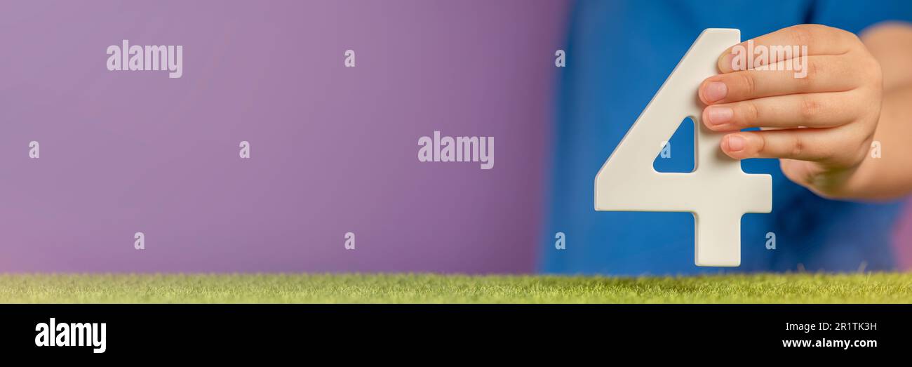 Number 4 in hand. Hand holding white number four over green grass and ...