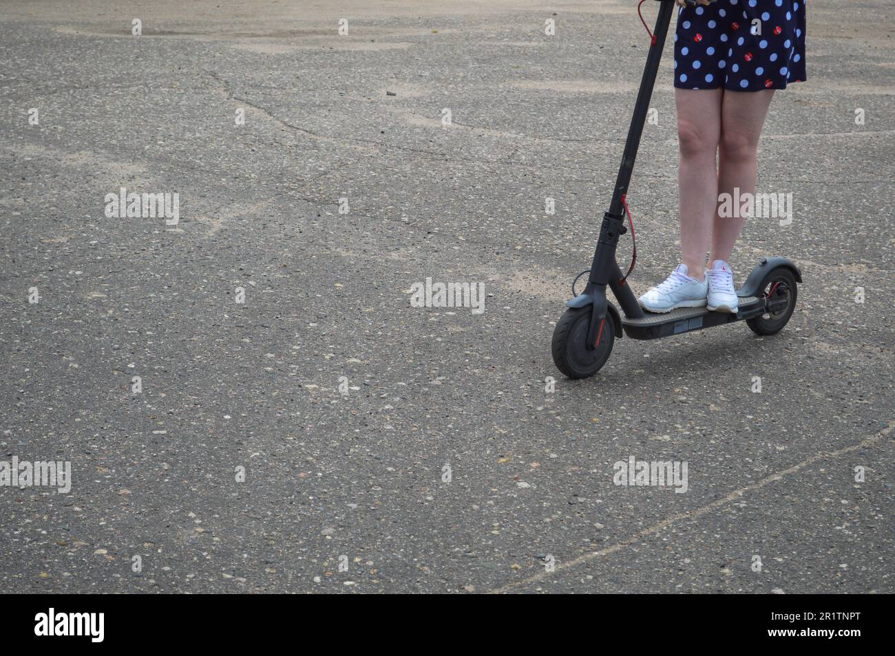 A girl woman in a short skirt and sneakers rides a trendy modern ...