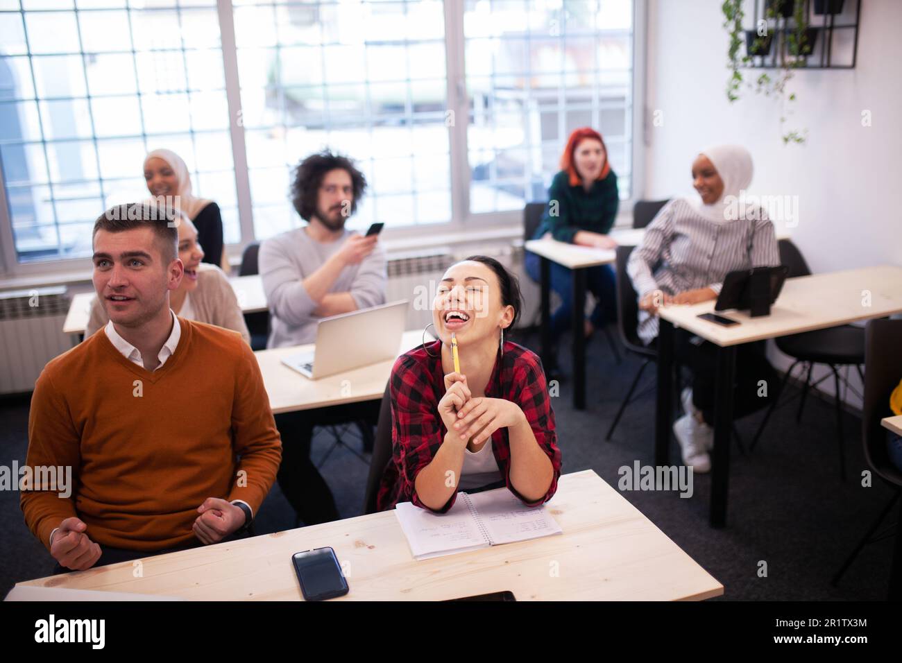 Multi ethnic students making fun of lecturer in a classroom behind his ...