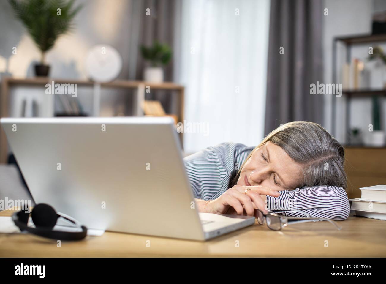 Elderly caucasian woman falling asleep at writing desk with portable ...