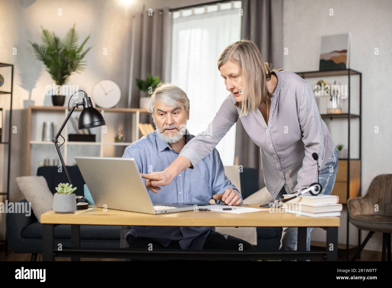 Middle-aged woman in business casual wear pointing at laptop screen ...