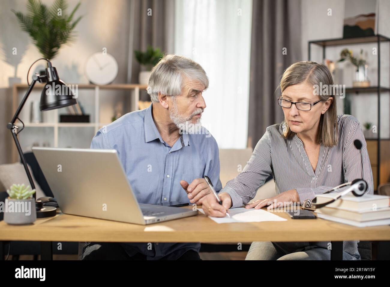 Middle-aged lady in glasses putting down information while senior male ...