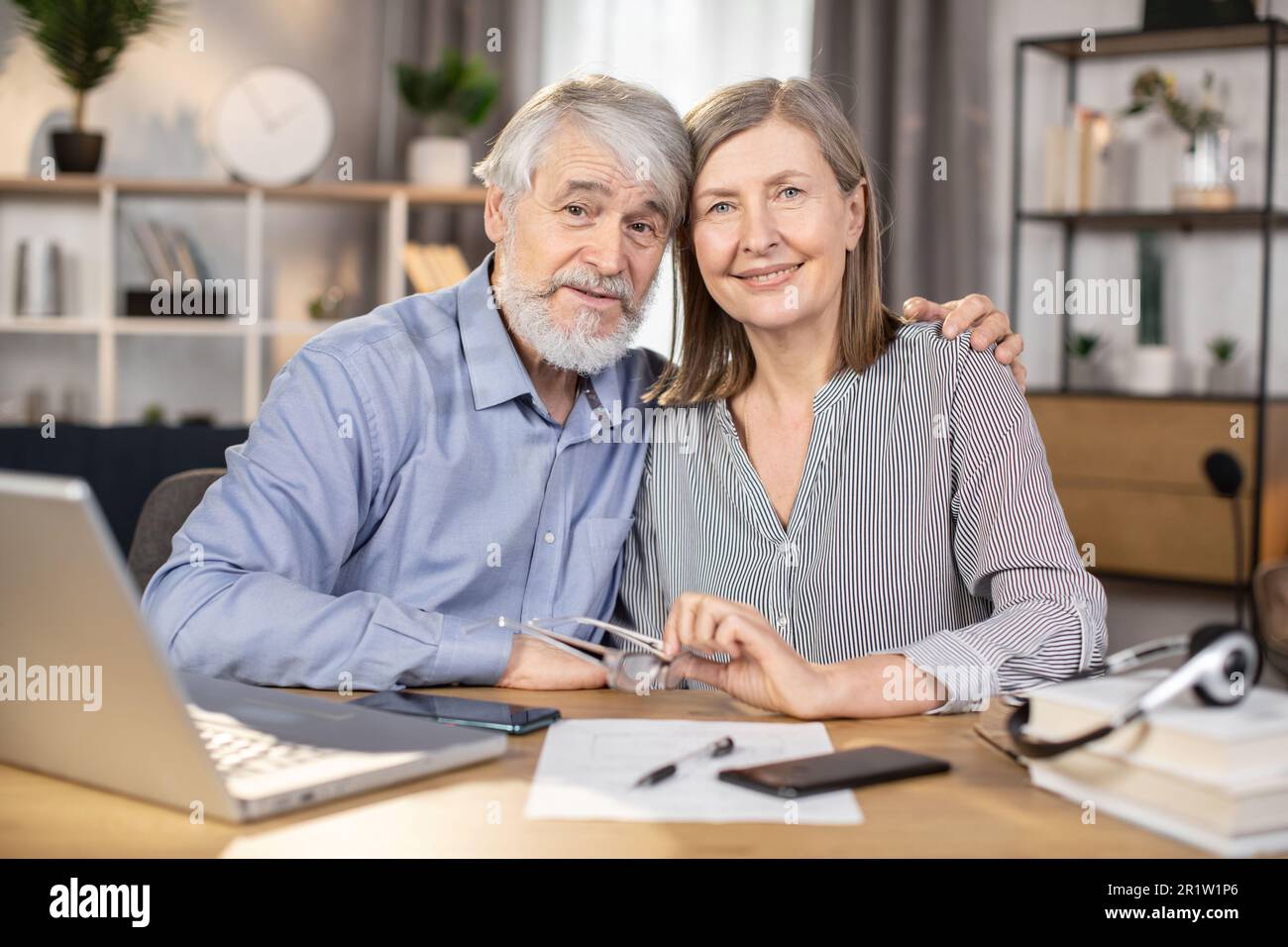 Portrait of happy couple of middle-aged people cuddling at office desk ...