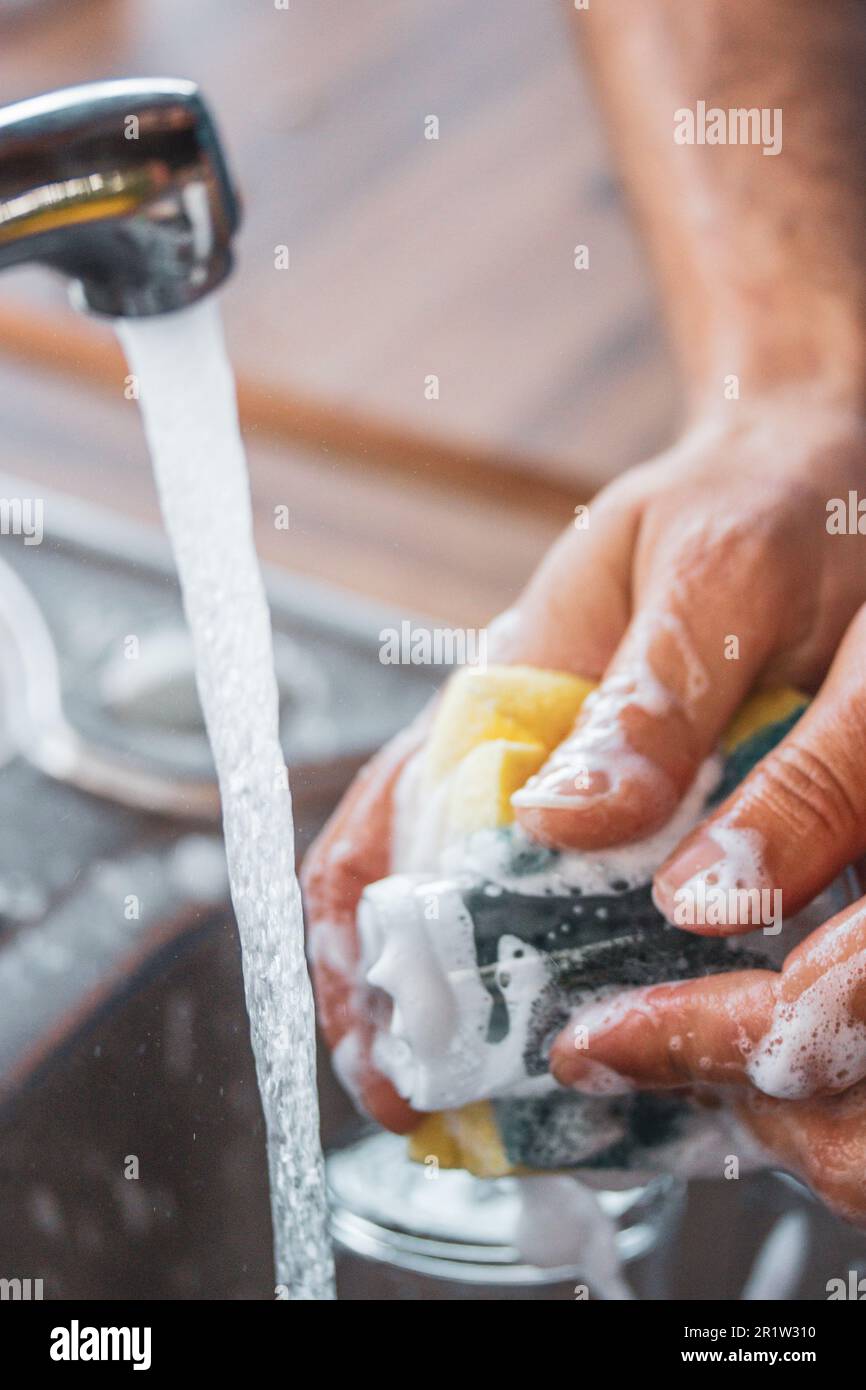 Man, human hands washing dishes, clear glass under a powerful stream of ...