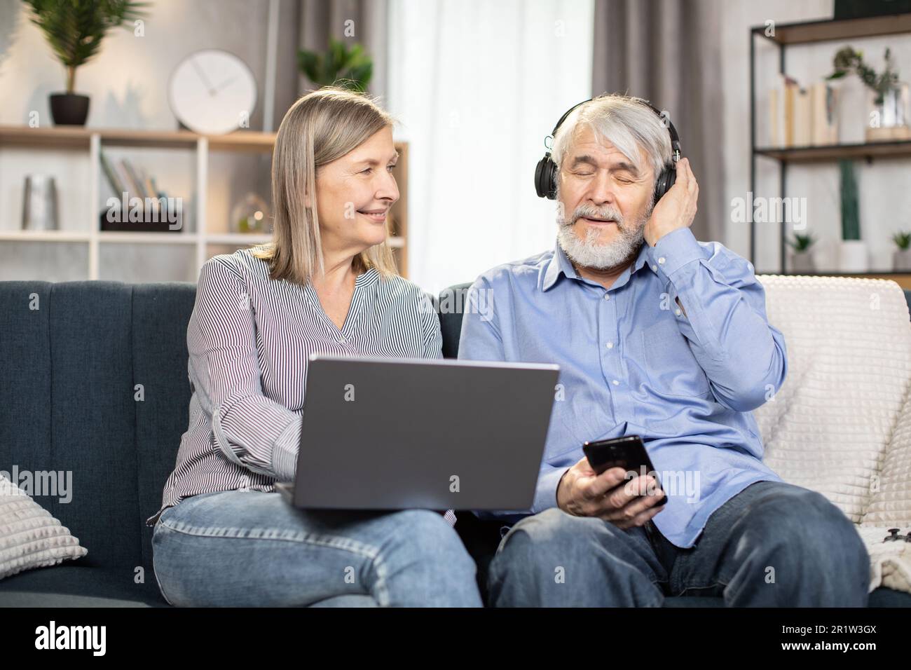 Cheerful senior pair having fun on comfortable sofa using modern laptop ...