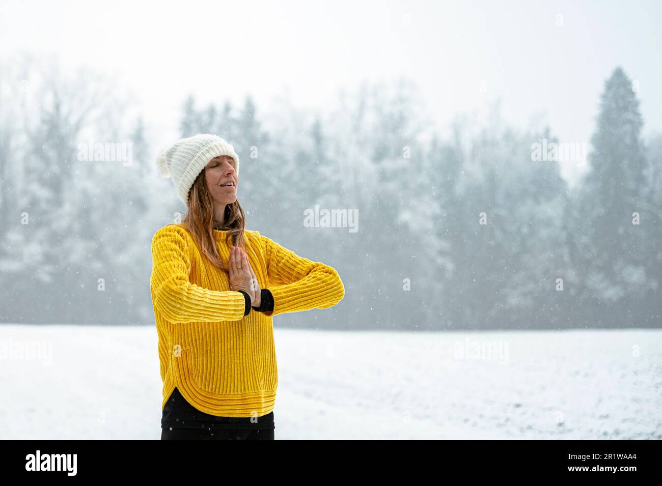 Serene young woman in yellow sweater praying or meditating standing in ...