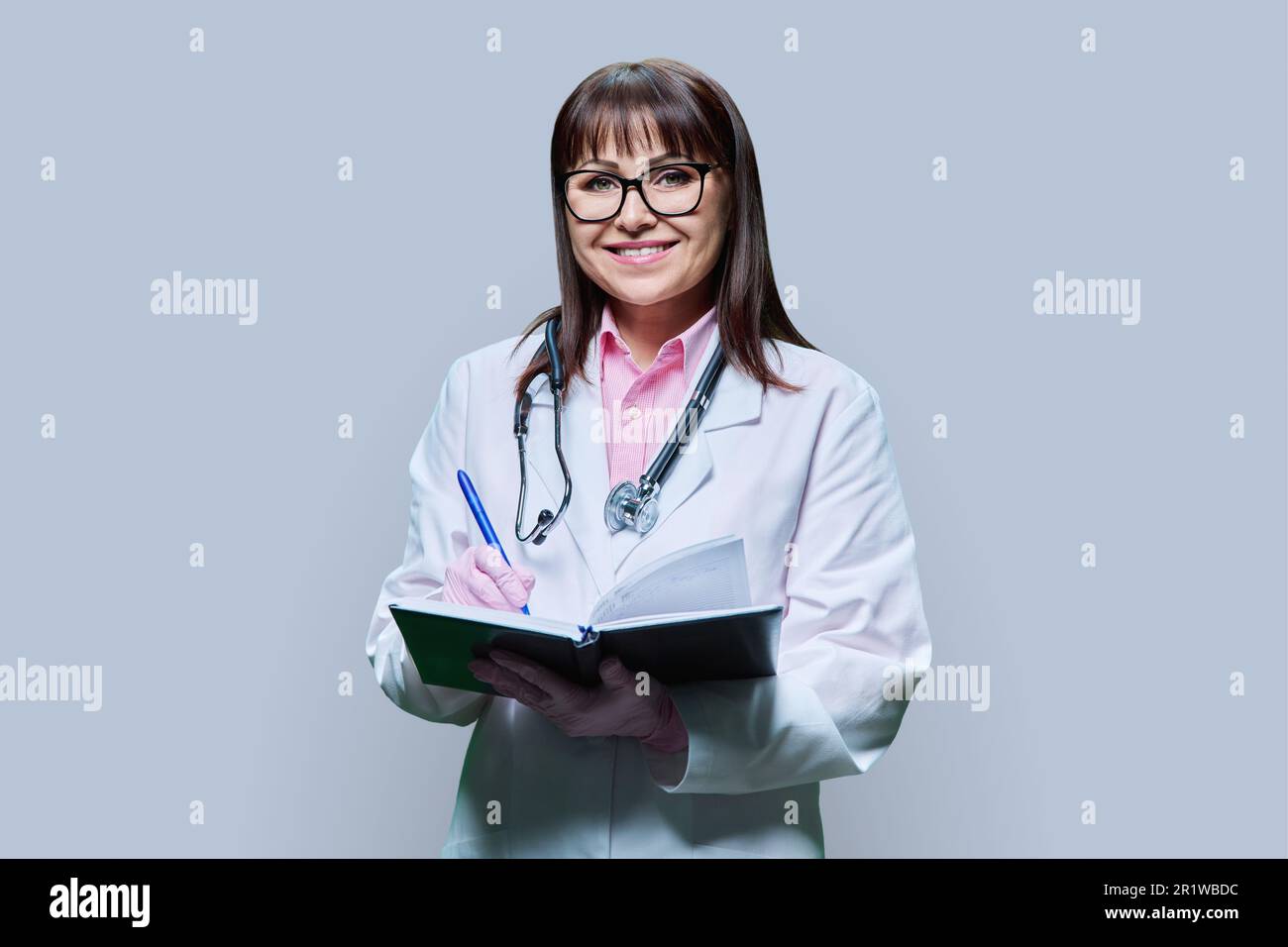 Female doctor taking note information in notebook on grey background ...