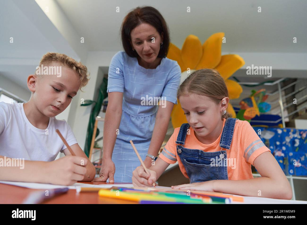 Creative kids during an art class in a daycare center or elementary school classroom drawing ...