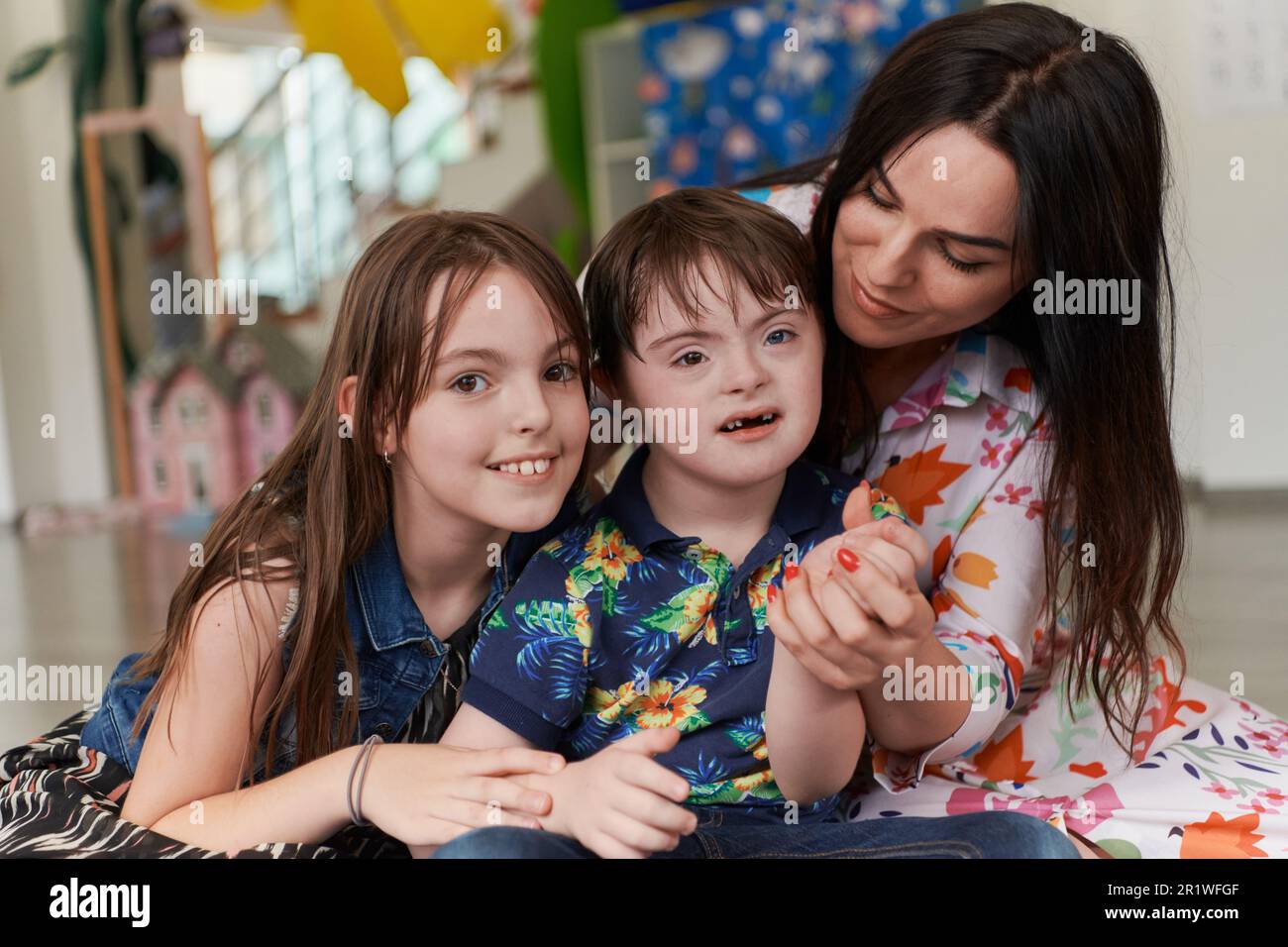 A girl and a woman hug a child with down syndrome in a modern preschool ...