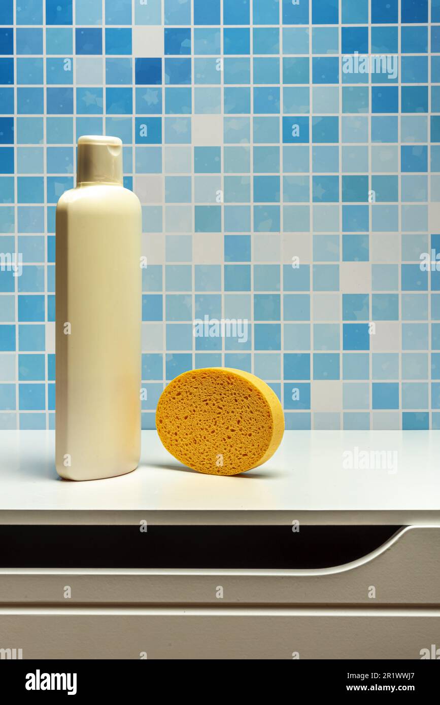 A bottle of bath shampoo along with a synthetic sponge on a white ...
