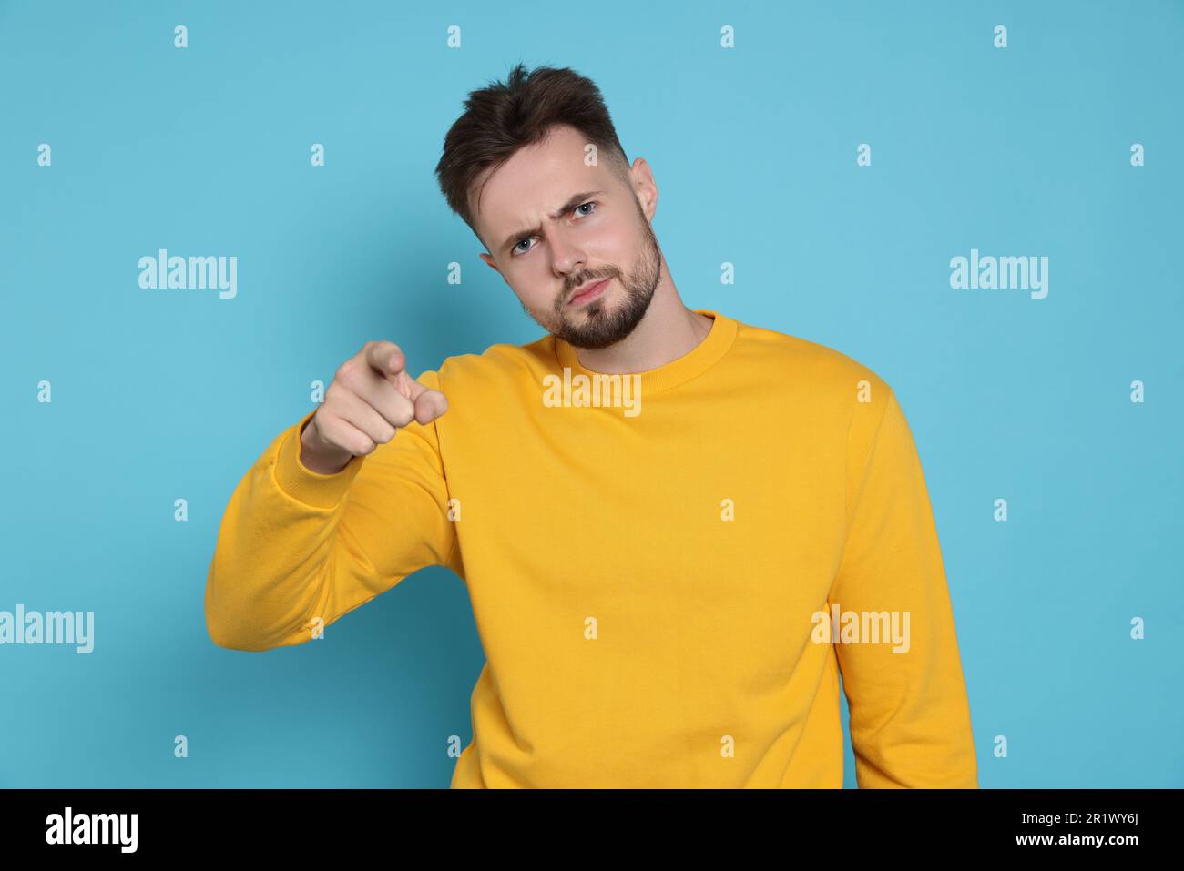 Aggressive man in yellow sweatshirt pointing at something on light blue ...