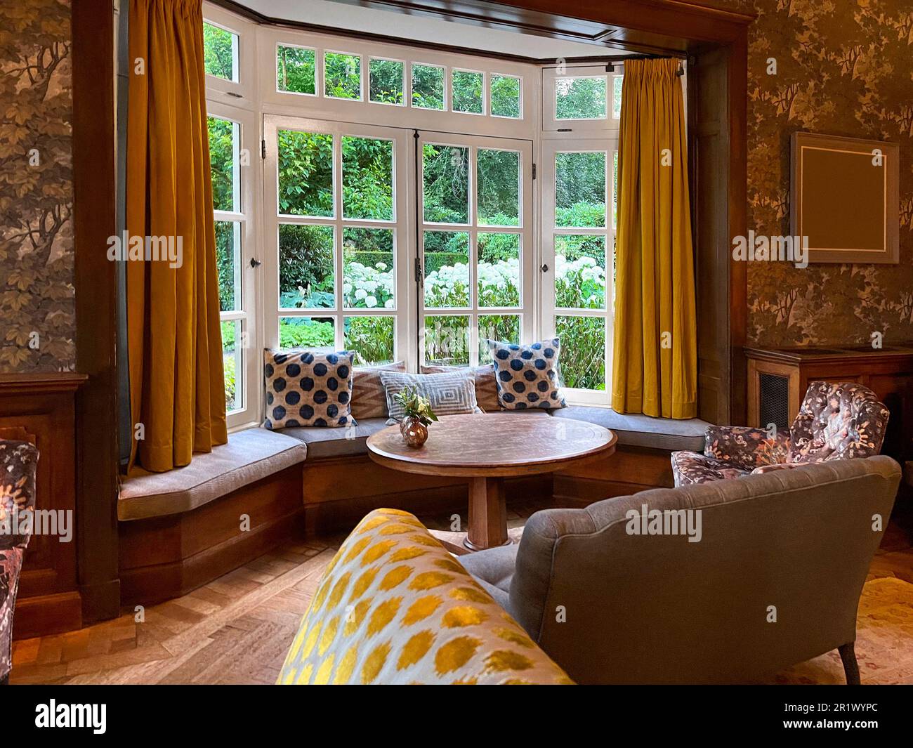 Wooden table near bay window seat with cushions in cozy room. Interior ...