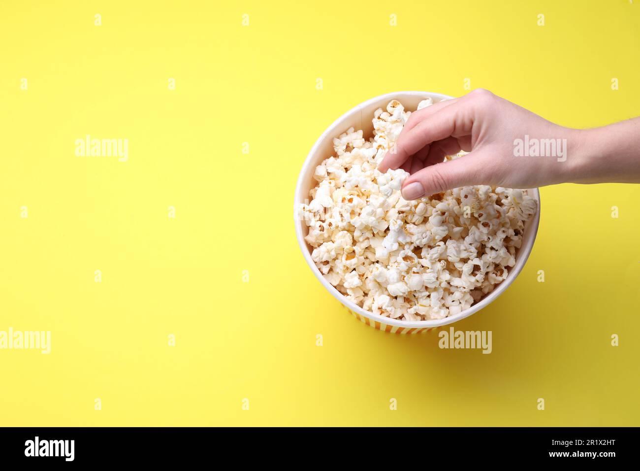 Woman taking delicious popcorn from paper bucket on yellow background ...