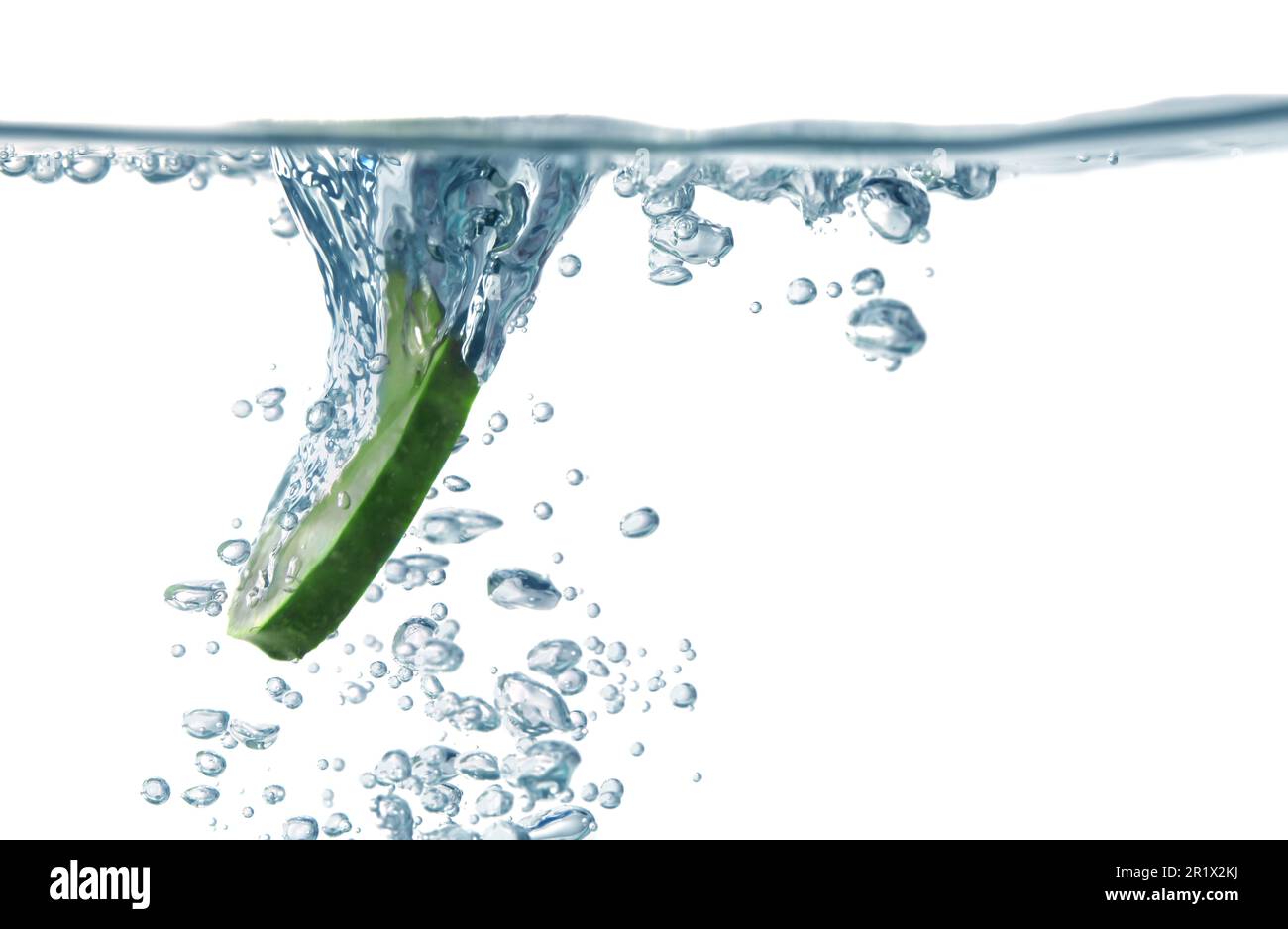Slice of fresh cucumber falling into glass with water on white ...
