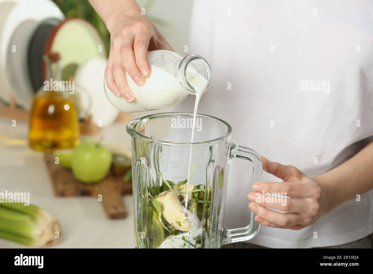 Woman adding milk into blender with ingredients for green smoothie ...