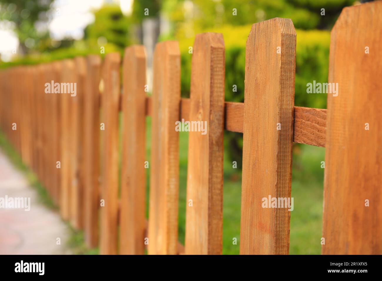 Closeup view of small wooden fence near green bush outdoors, space for ...