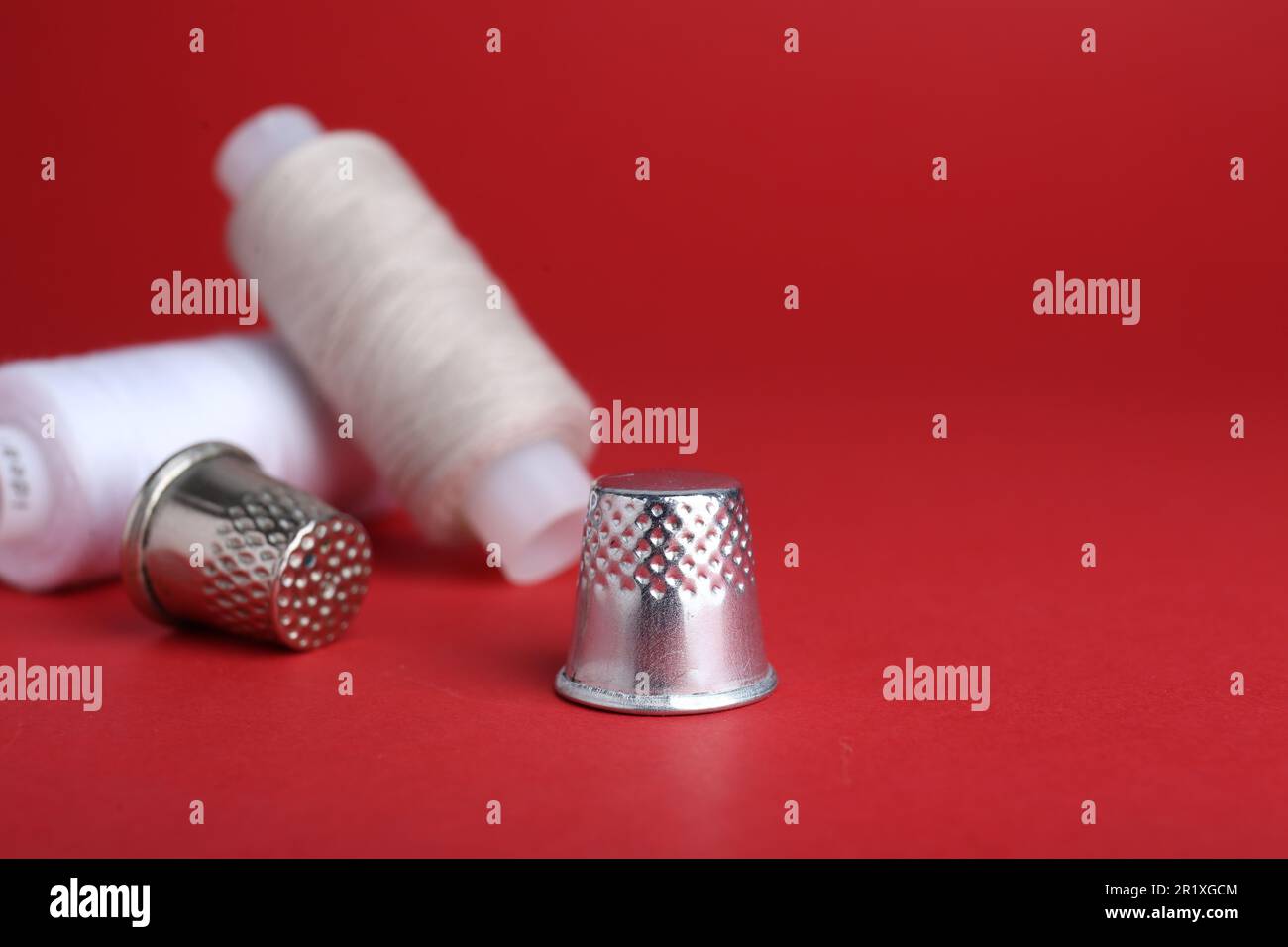 Silver thimbles and light thread on red background. Sewing accessories ...