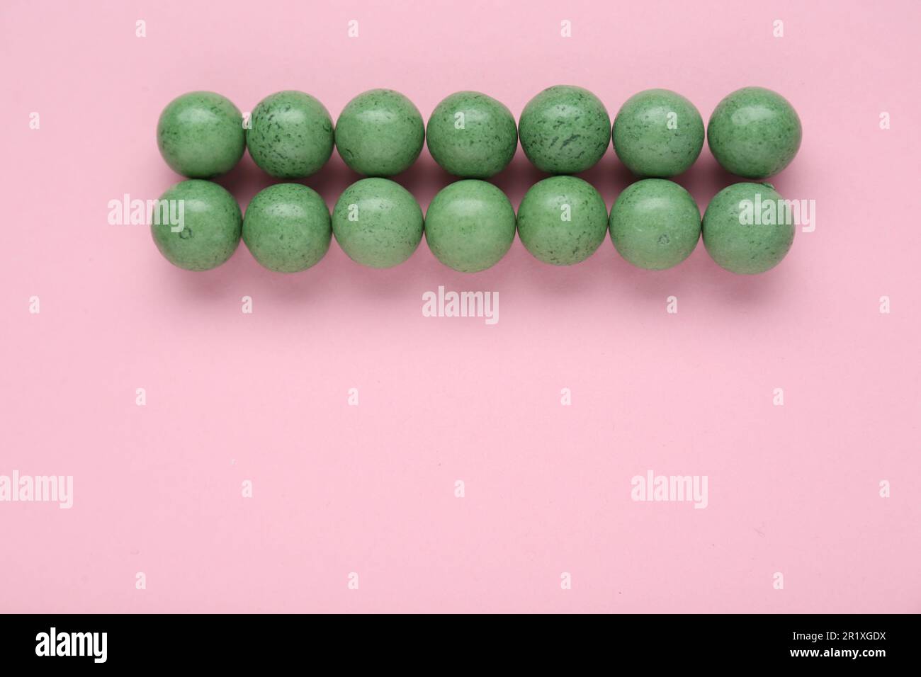 Many bright green gumballs on pink background, flat lay. Space for text ...