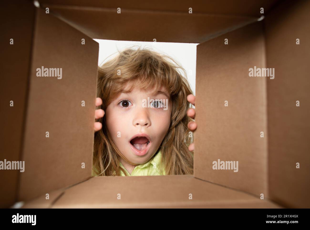 Happy little child boy is opening gift and looking inside cardboard box ...