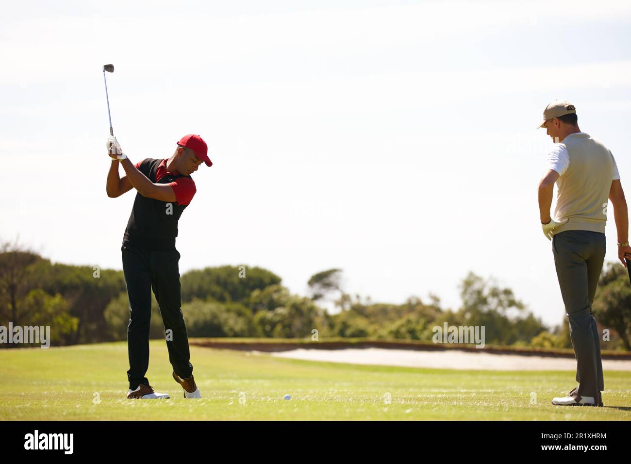 Helping him with his technique. two handsome men playing a game of golf ...
