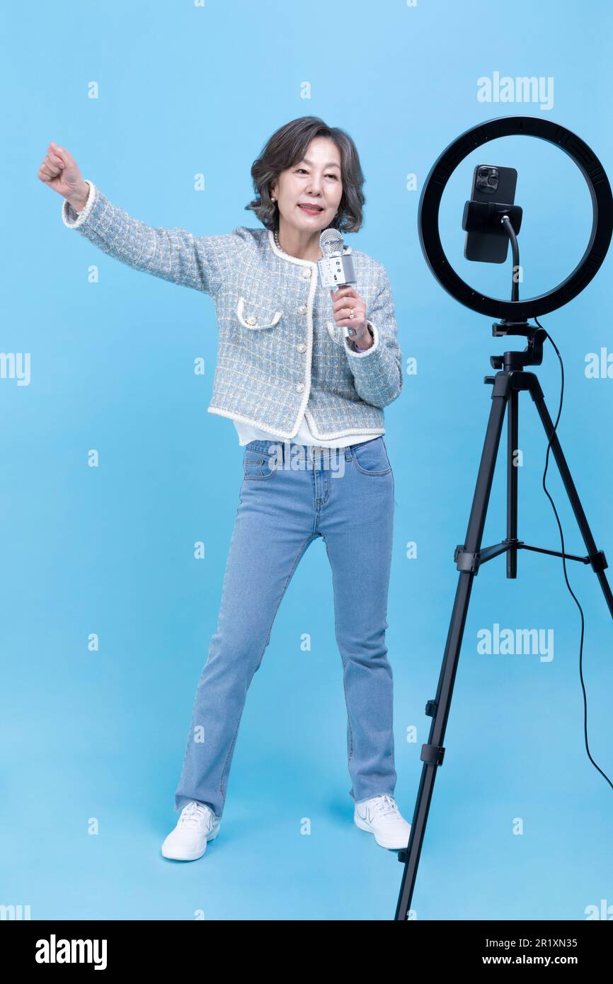 singing active young senior Korean Asian woman with smartphone, mobile ...