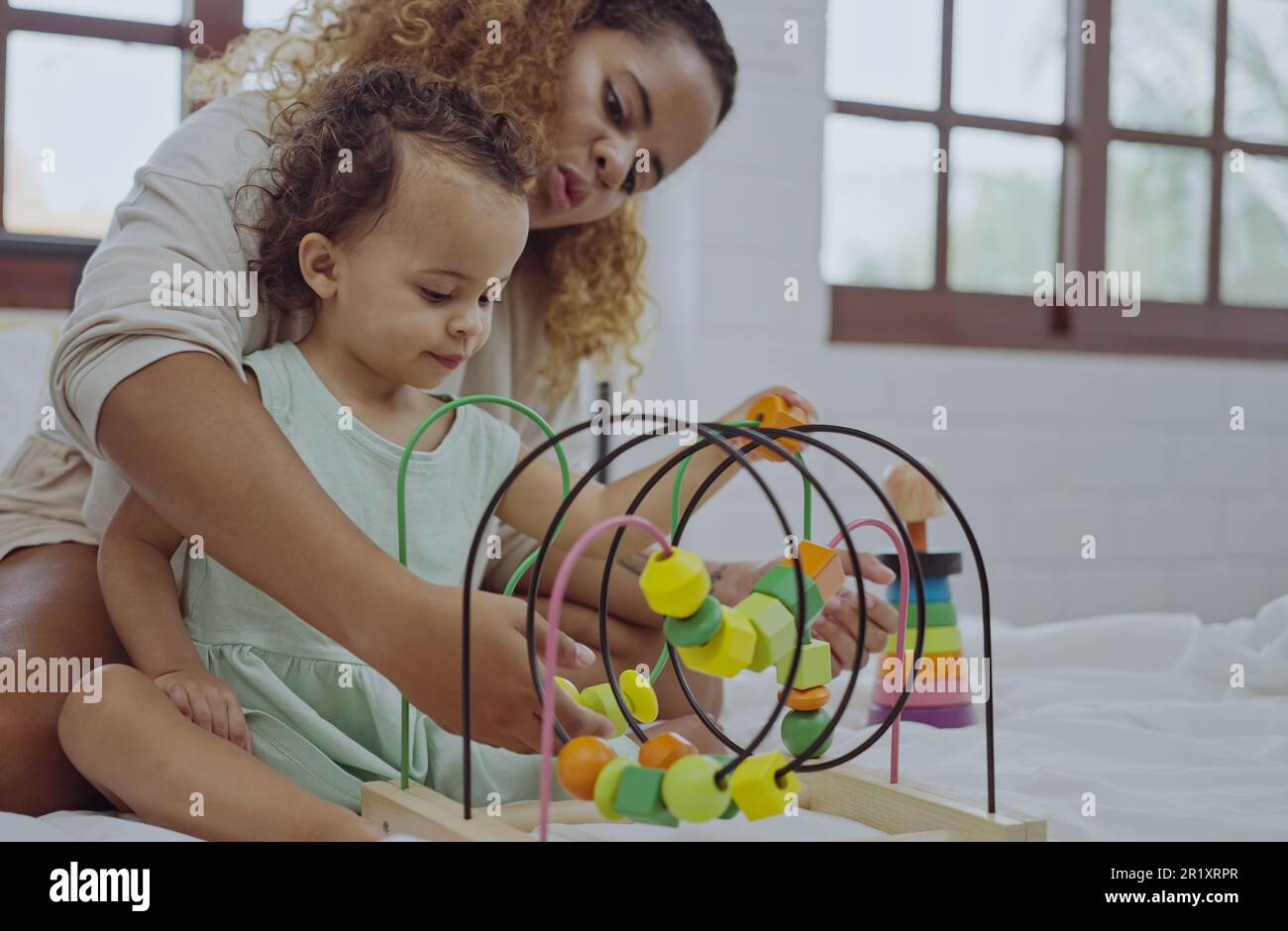 Happy mother and daughter playing with a toy developing colorful wooden blocks on bed together ...