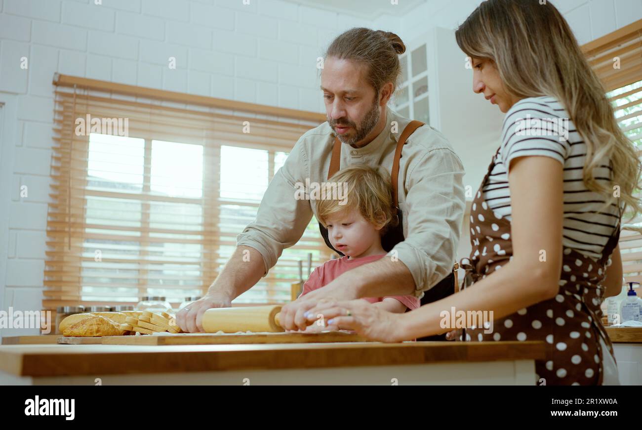 Father and mother teaching baby son kneading dough on kitchen counter ...