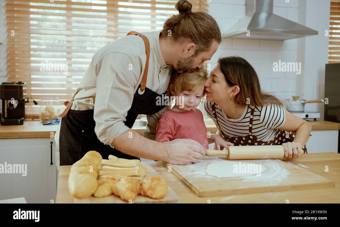 Father and mother teaching baby son kneading dough on kitchen counter ...