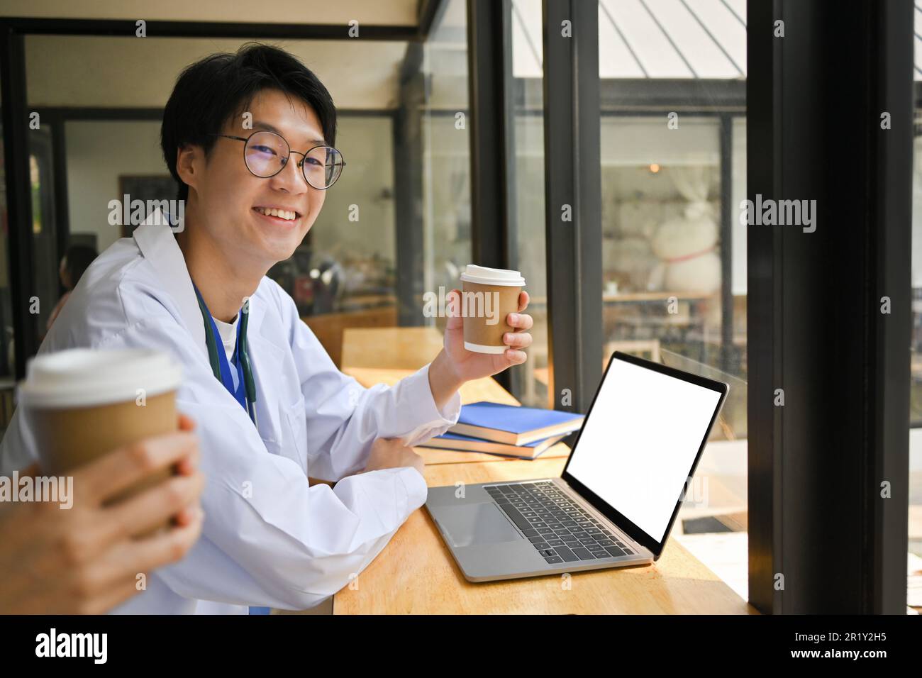 Smiling male doctor in white uniform holding paper cup of coffee ...