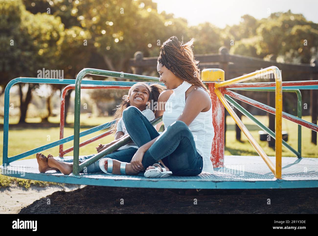 Woman, young girl together on roundabout at park and playing with smile ...