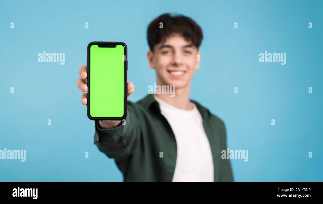 Young man smiling and showing his phone with green screen into the ...