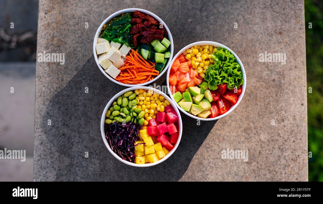 Close vertical view of three poke bowls with vegetables, fruits, fish ...