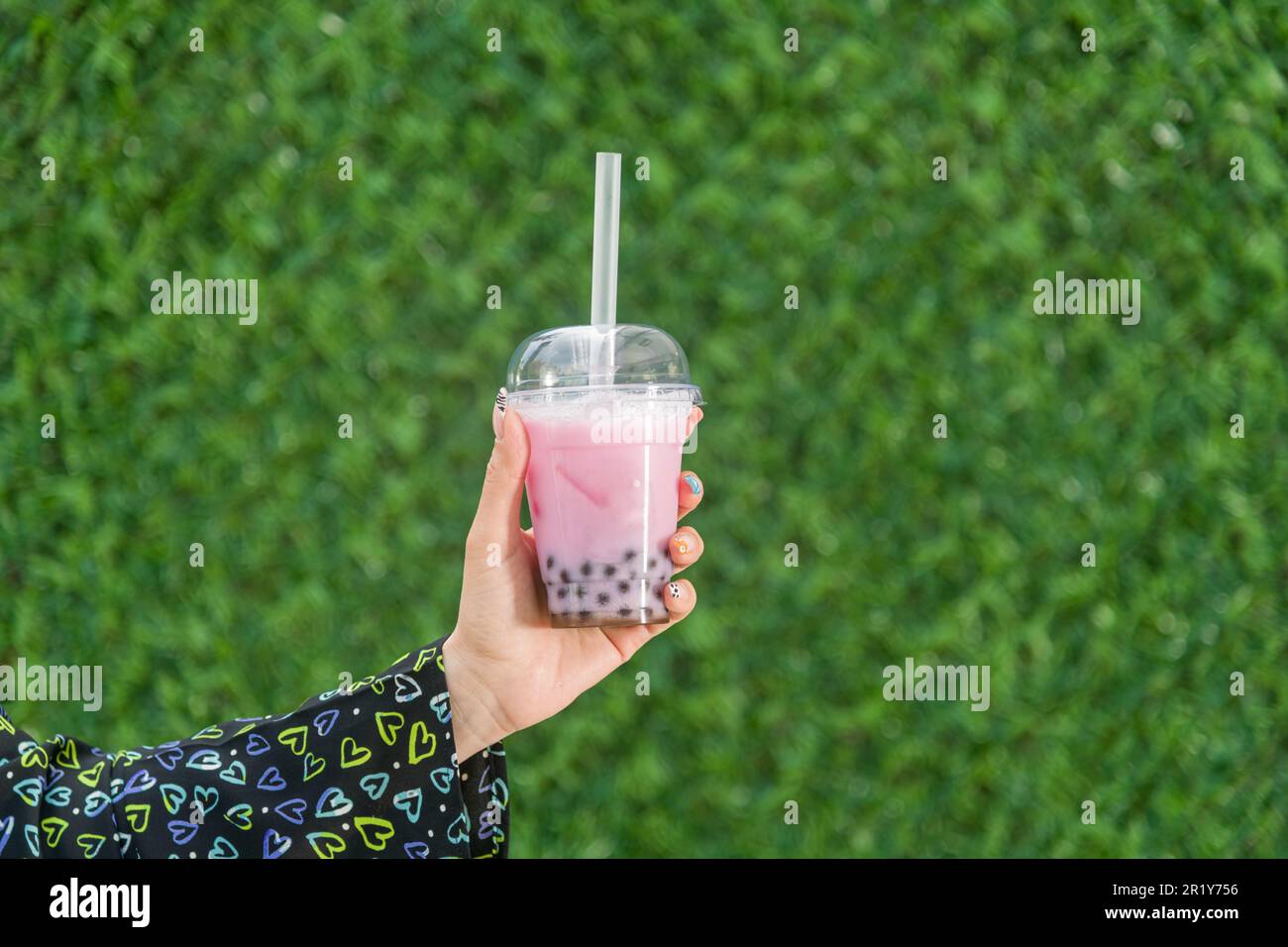 Woman holding bubble tea with lemonade in front of green grass wall ...