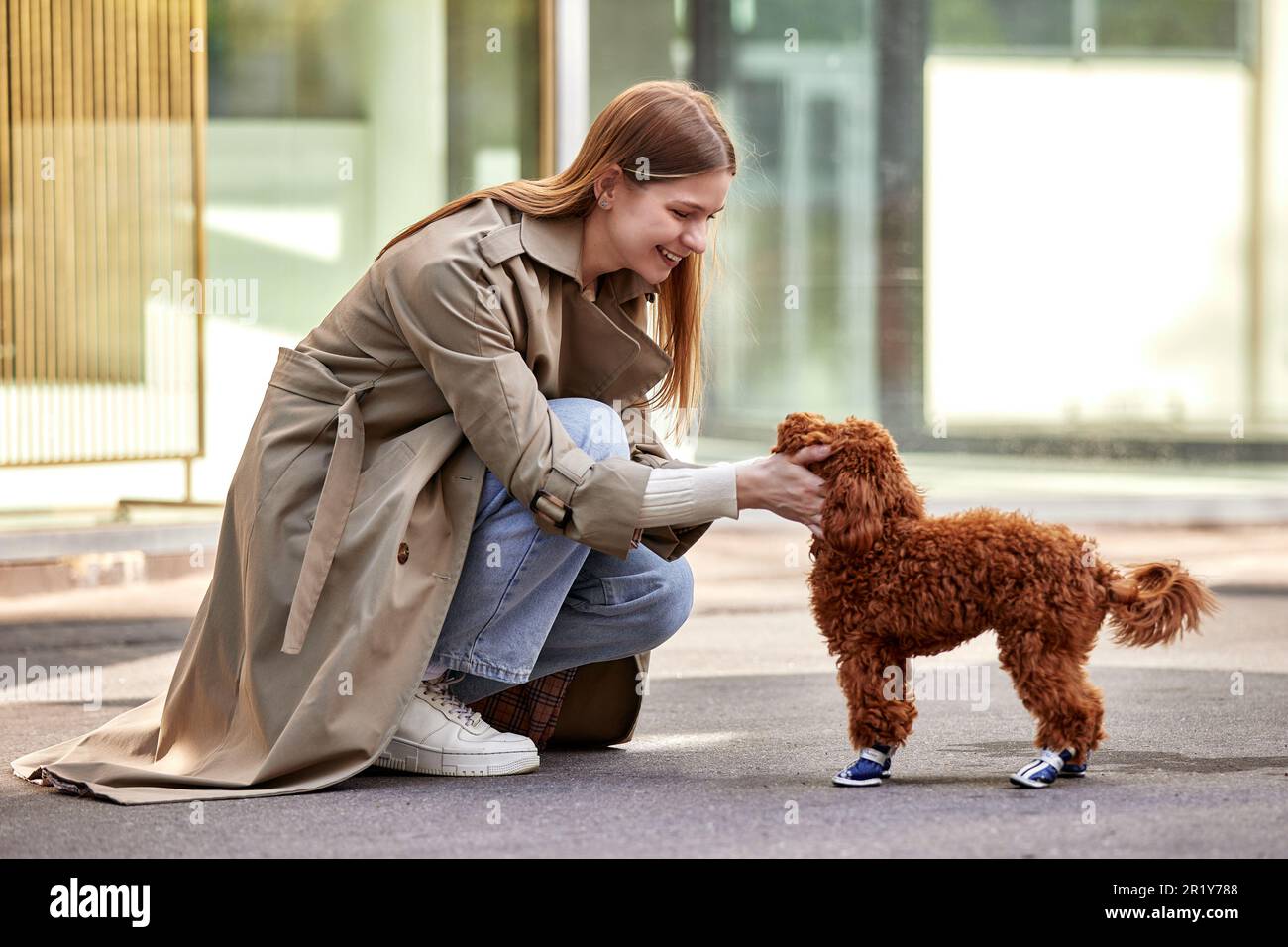 A young smiling girl in a stylish beige raincoat on a walk with her ...