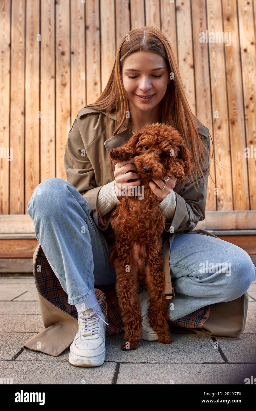 A young smiling blonde girl in jeans and a beige raincoat sits and ... A young smiling blonde girl in jeans and a beige raincoat sits and ...