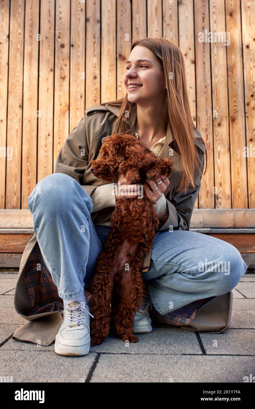 A young smiling blonde girl in jeans and a beige raincoat sits and ... A young smiling blonde girl in jeans and a beige raincoat sits and ...