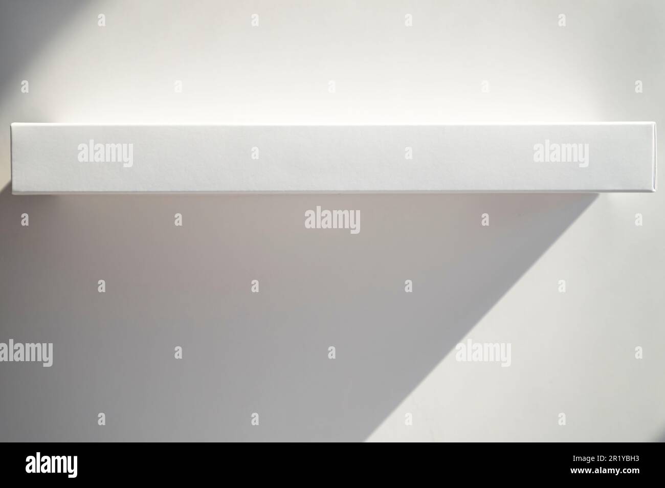 Long thin cardboard white box on paper surface with shadows and ...