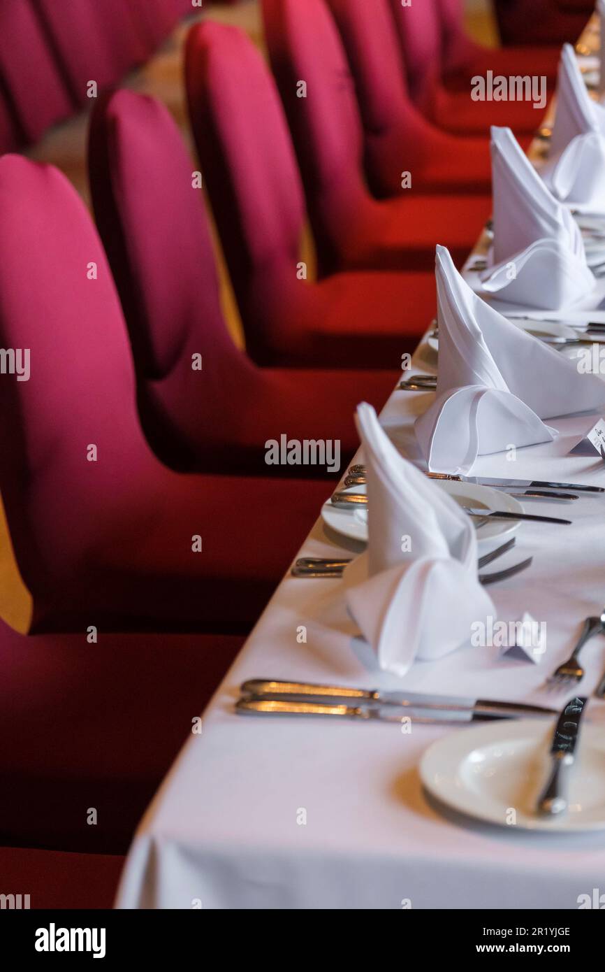 A long dining table set out for a large party with red chairs and white ...