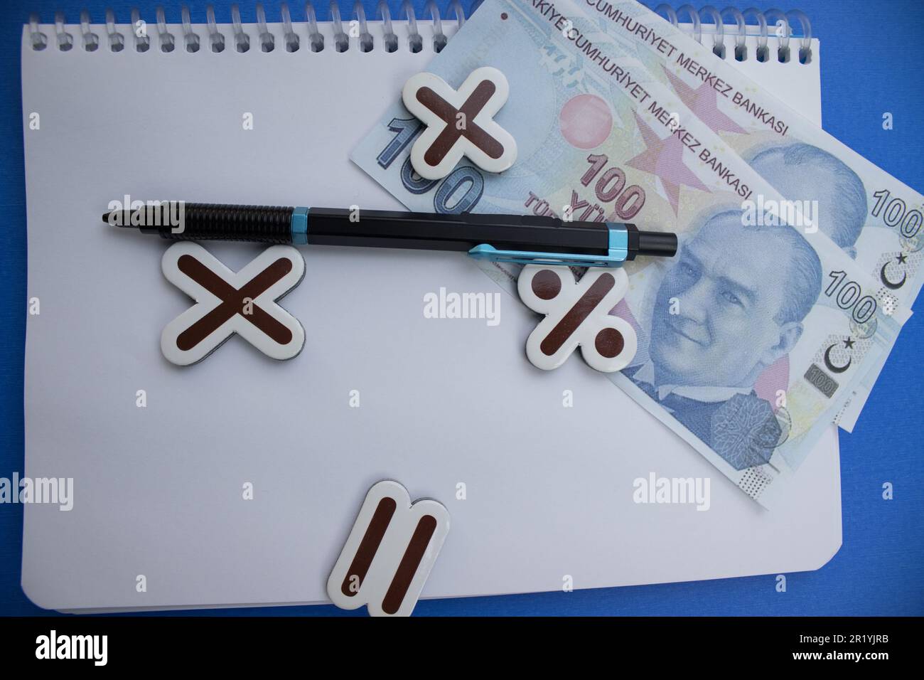 A notebook, Turkish liras, pens and math signs are placed on a blue ...