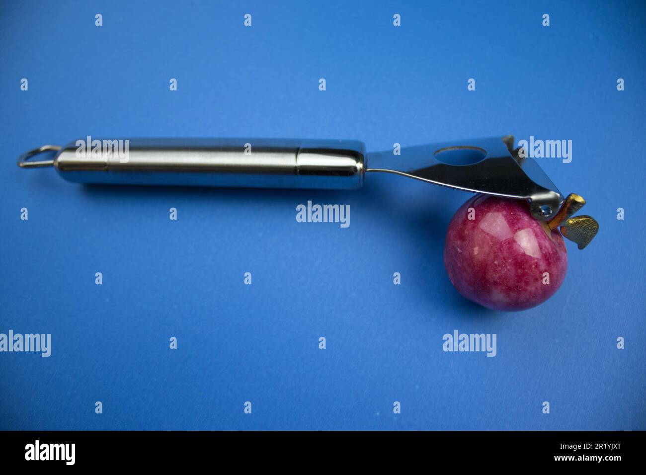 Placed on a blue background, a fruit peeler and a red-colored stone ...